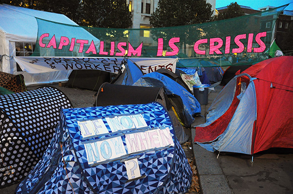 protest encampment with banner saying Capitalism is Crisis